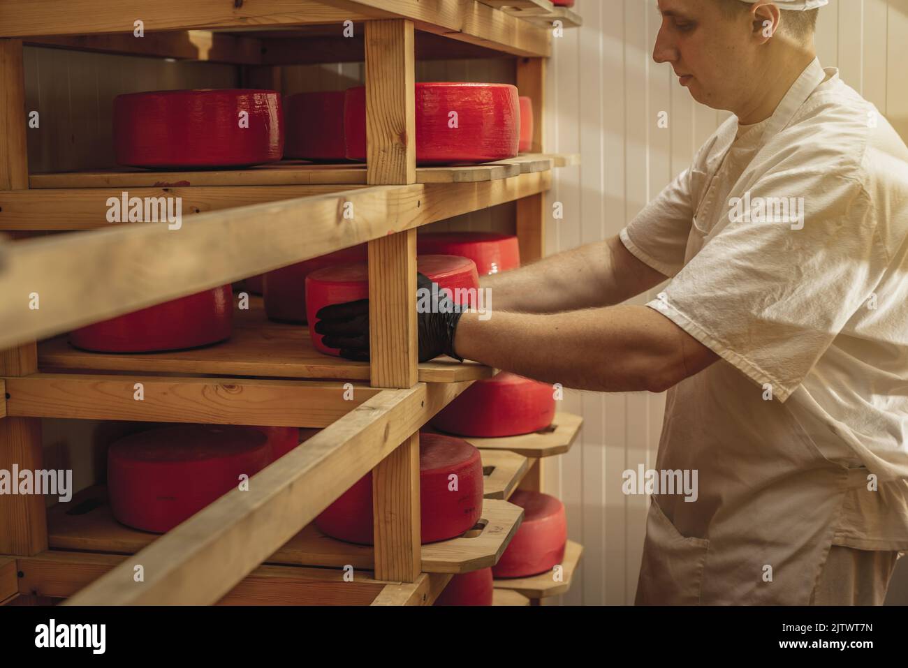 A farmer turns over cheese heads on wooden shelves in the cheese ...