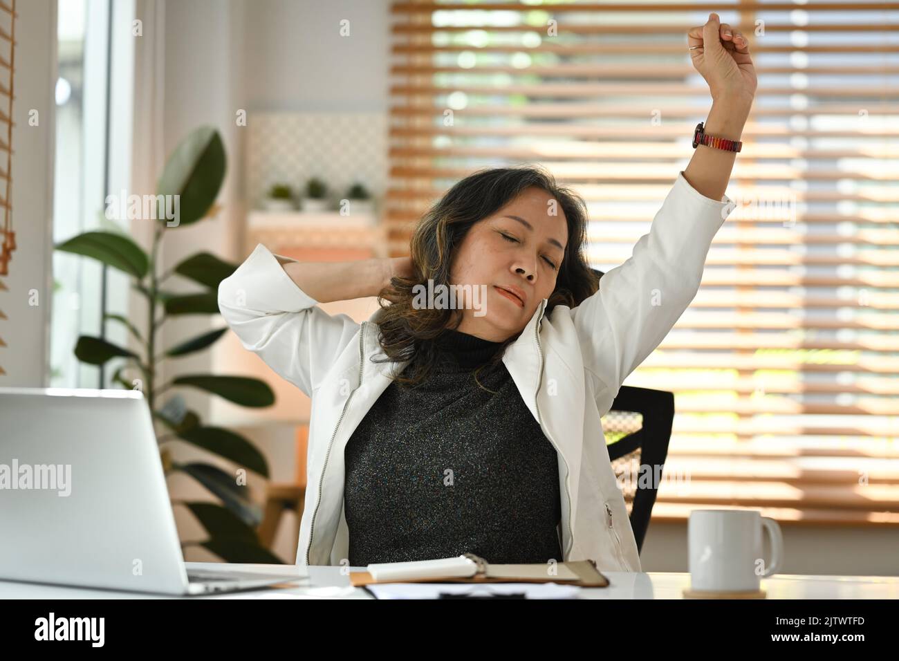 Satisfied middle aged woman stretching her body, resting at workplace ...