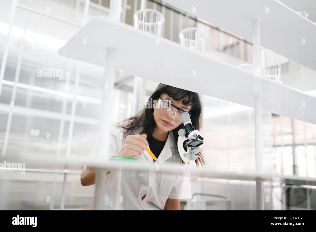 Young scientist in white lab coat working with binocular microscope in ...