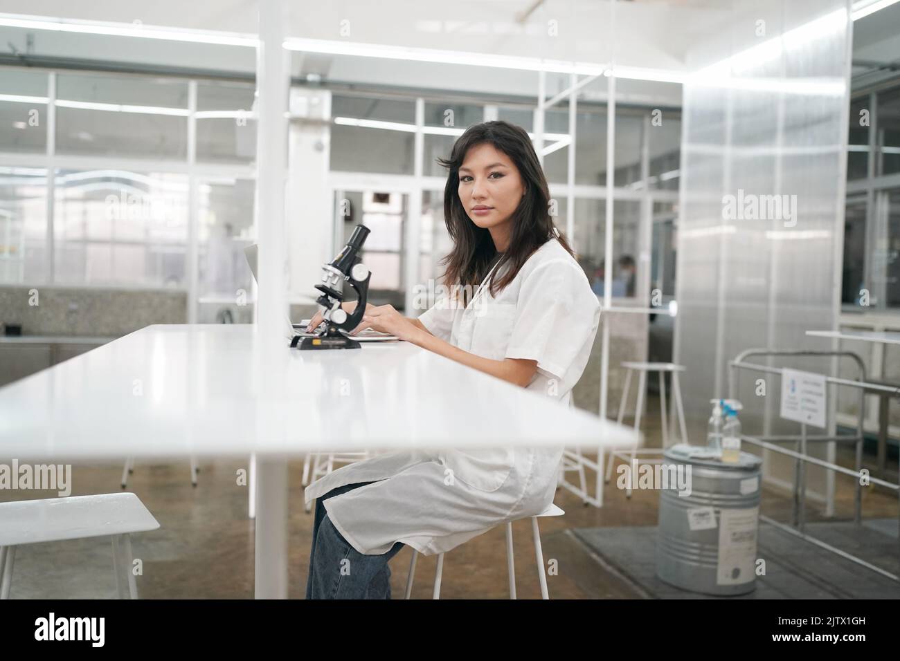 Young scientist in white lab coat working with binocular microscope in the material science lab ...