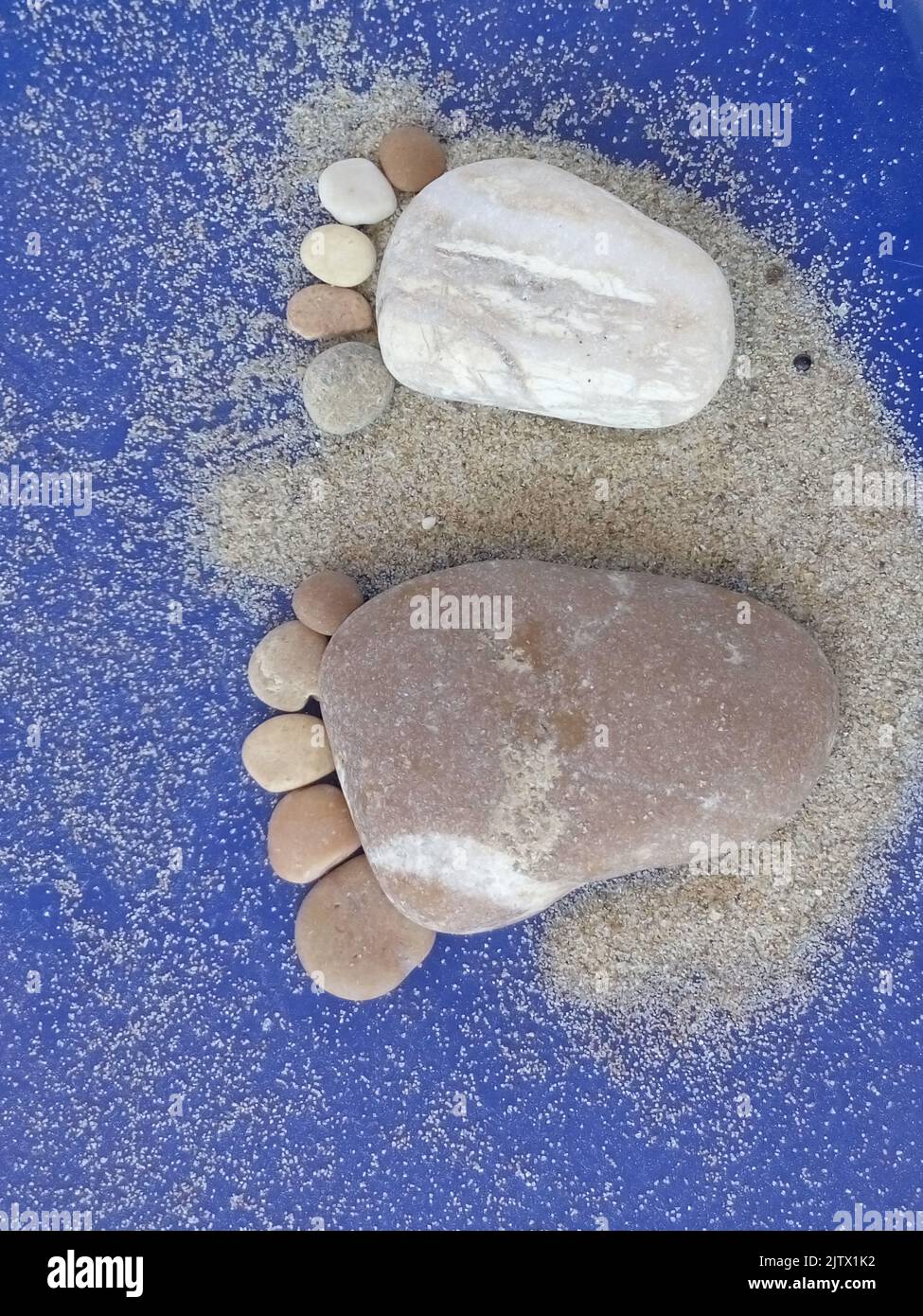 Baby feet shape made with pebbles on the beach with sand and blue ...