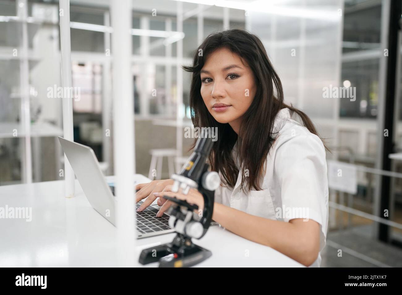 Young scientist in white lab coat working with binocular microscope in ...