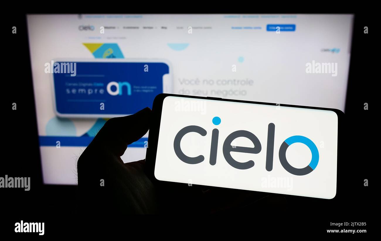 Person holding mobile phone with logo of Brazilian payments company Cielo SA on screen in front ...