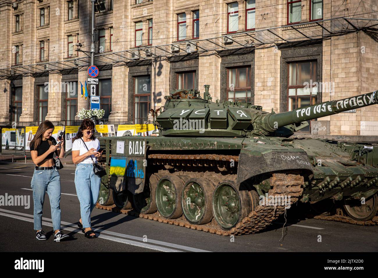 Two women walk past a demolished Russian tank repainted with slogans ...