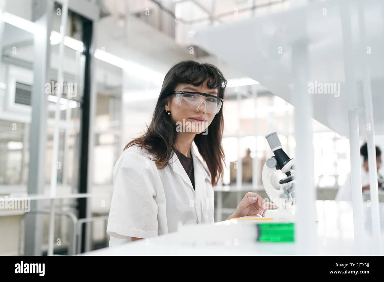 Young scientist in white lab coat working with binocular microscope in ...