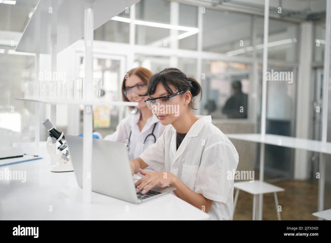 Young scientist in white lab coat working with binocular microscope in ...