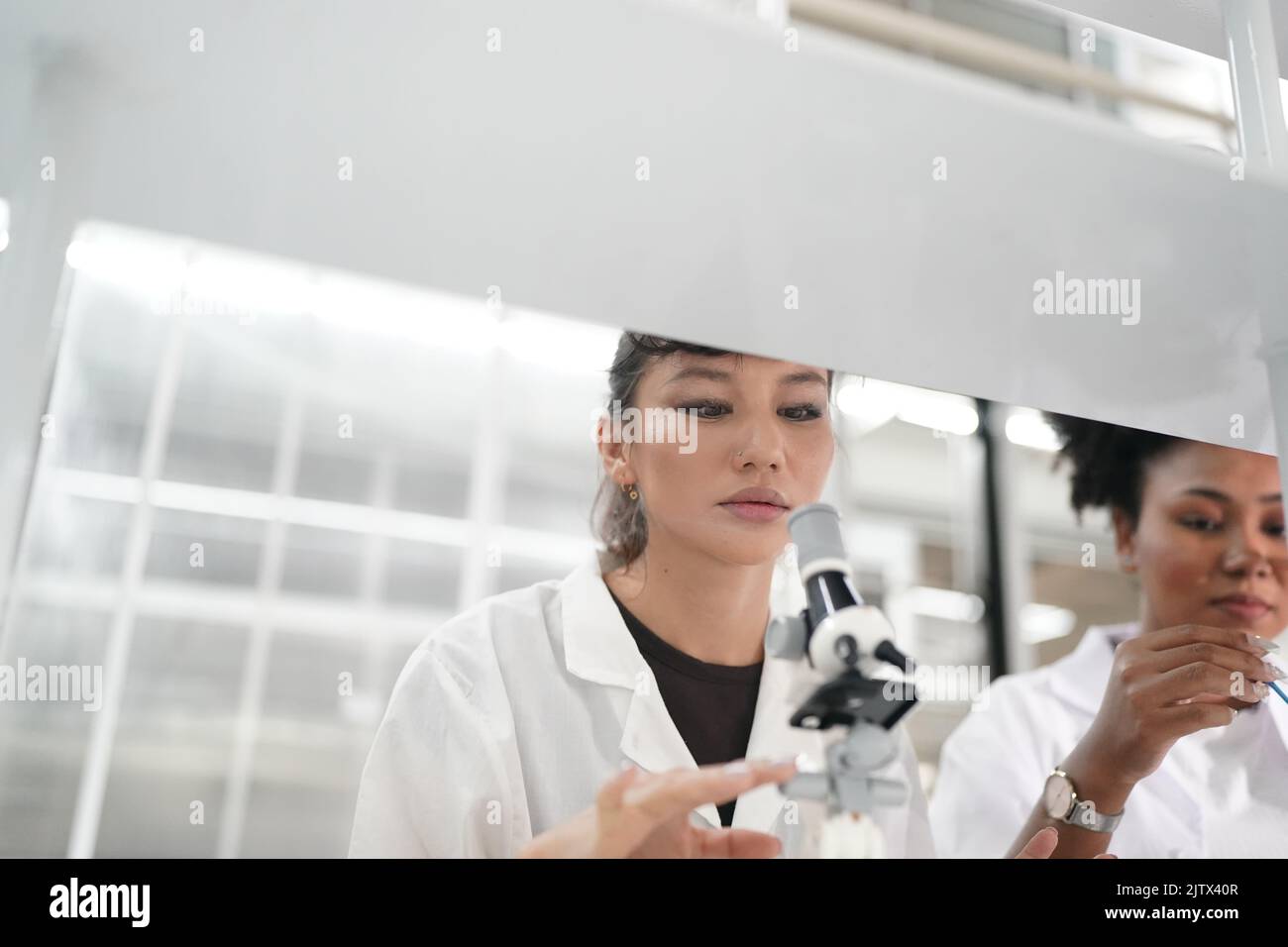 Young scientist in white lab coat working with binocular microscope in ...