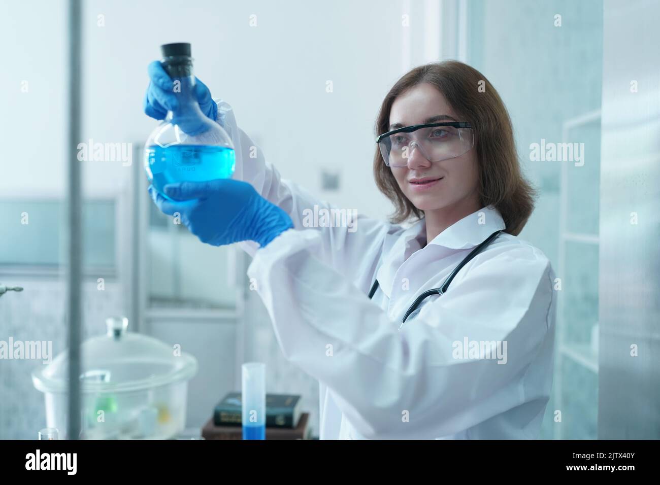 Young scientist in white lab coat working with binocular microscope in the material science lab ...