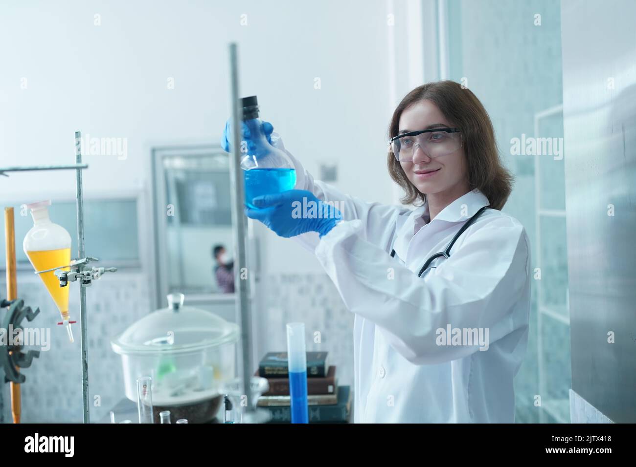 Young scientist in white lab coat working with binocular microscope in ...