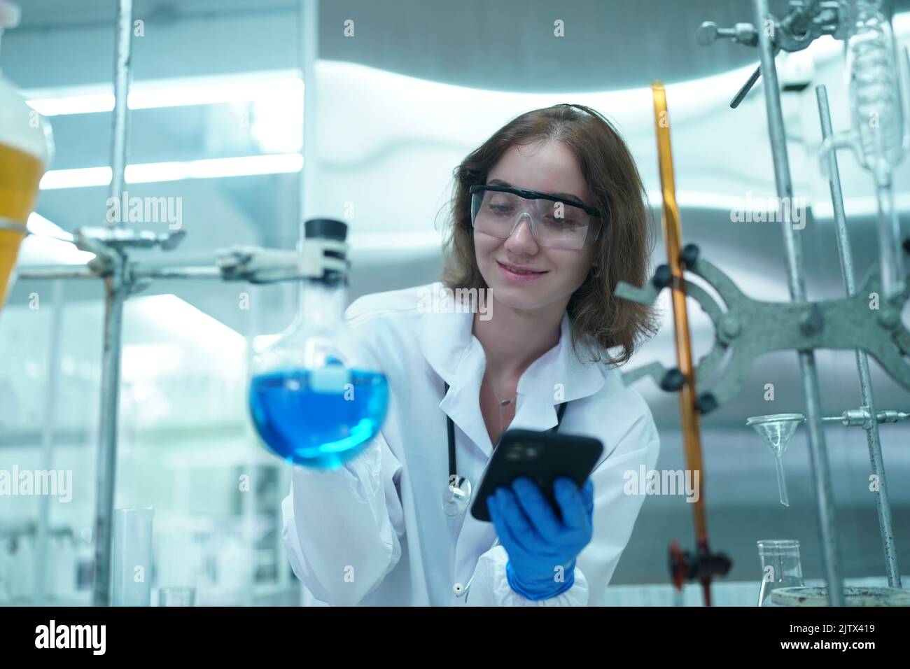 Young scientist in white lab coat working with binocular microscope in the material science lab ...