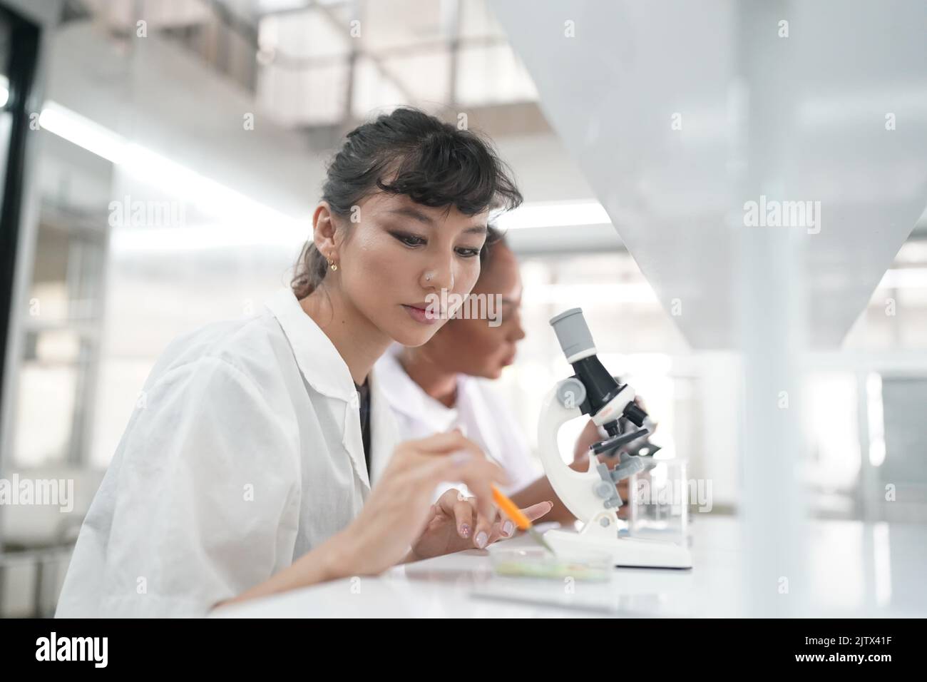 Young scientist in white lab coat working with binocular microscope in ...