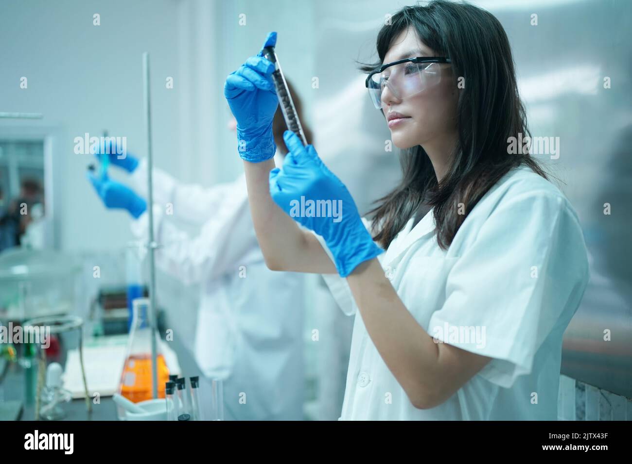 Young scientist in white lab coat working with binocular microscope in ...