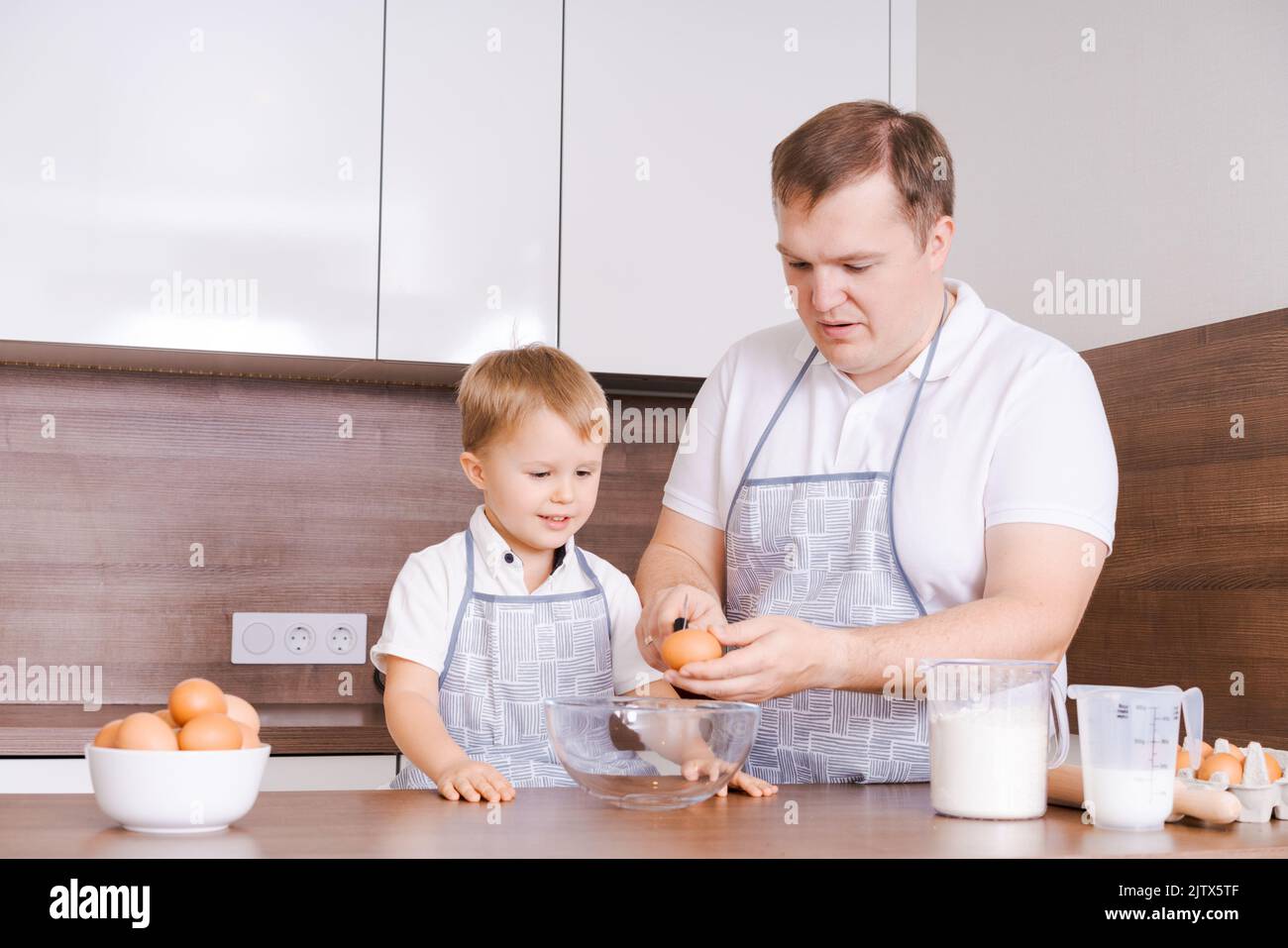 Dad and son in kitchen, father teaches child to break eggs into a bowl ...
