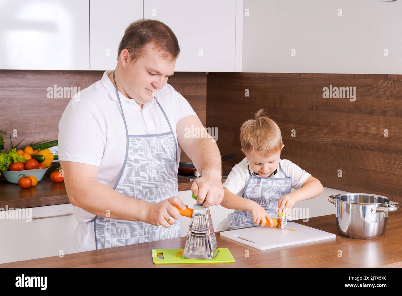 Father cooks with his son, rub carrots on grater at home in the kitchen ...