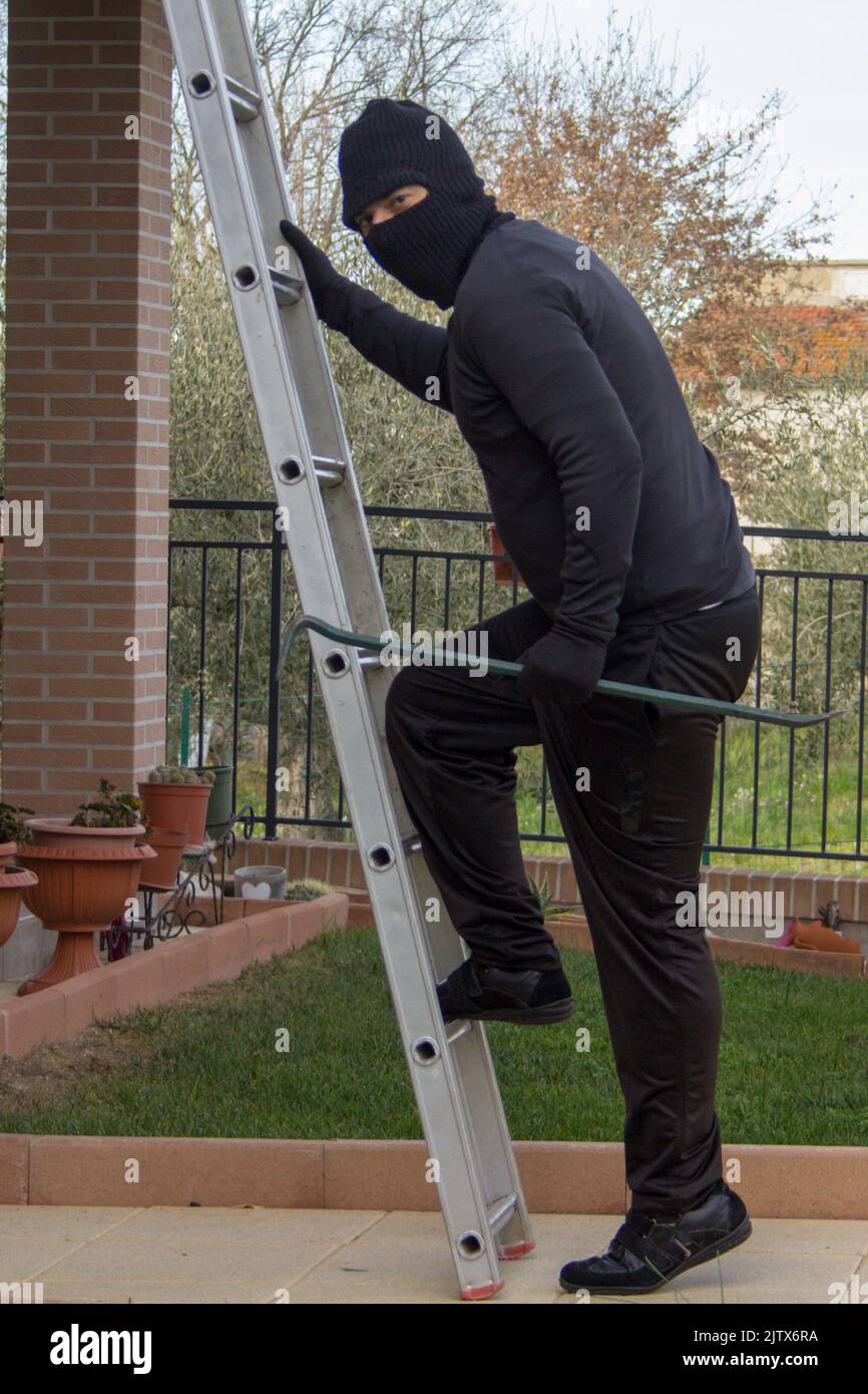 thief dressed in black with a crowbar climbing a ladder trying to sneak ...
