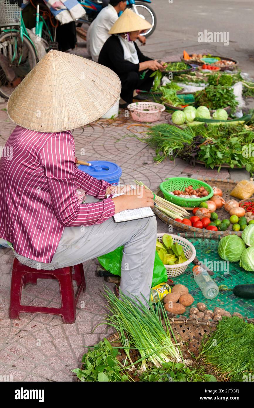 Vietnamese lady wearing bamboo hat selling vegetables in street market ...