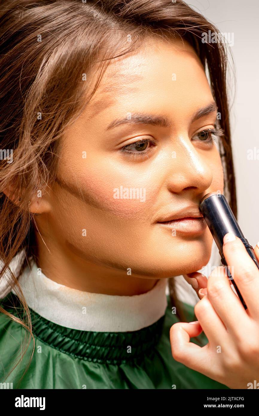 Beautiful young brunette woman receiving makeup with stick concealer on ...