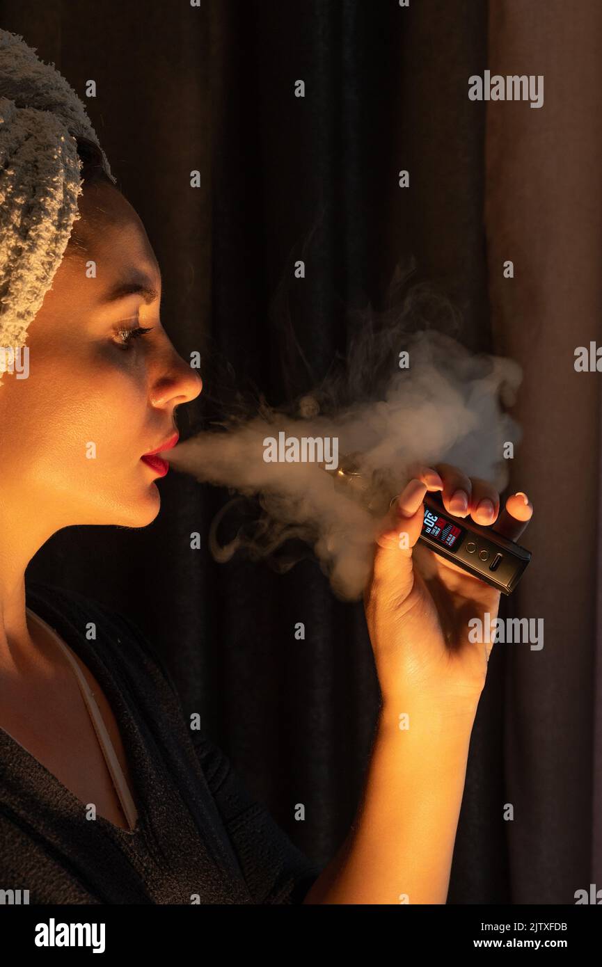A girl smokes an electronic cigarette and exhales smoke, her lips are ...