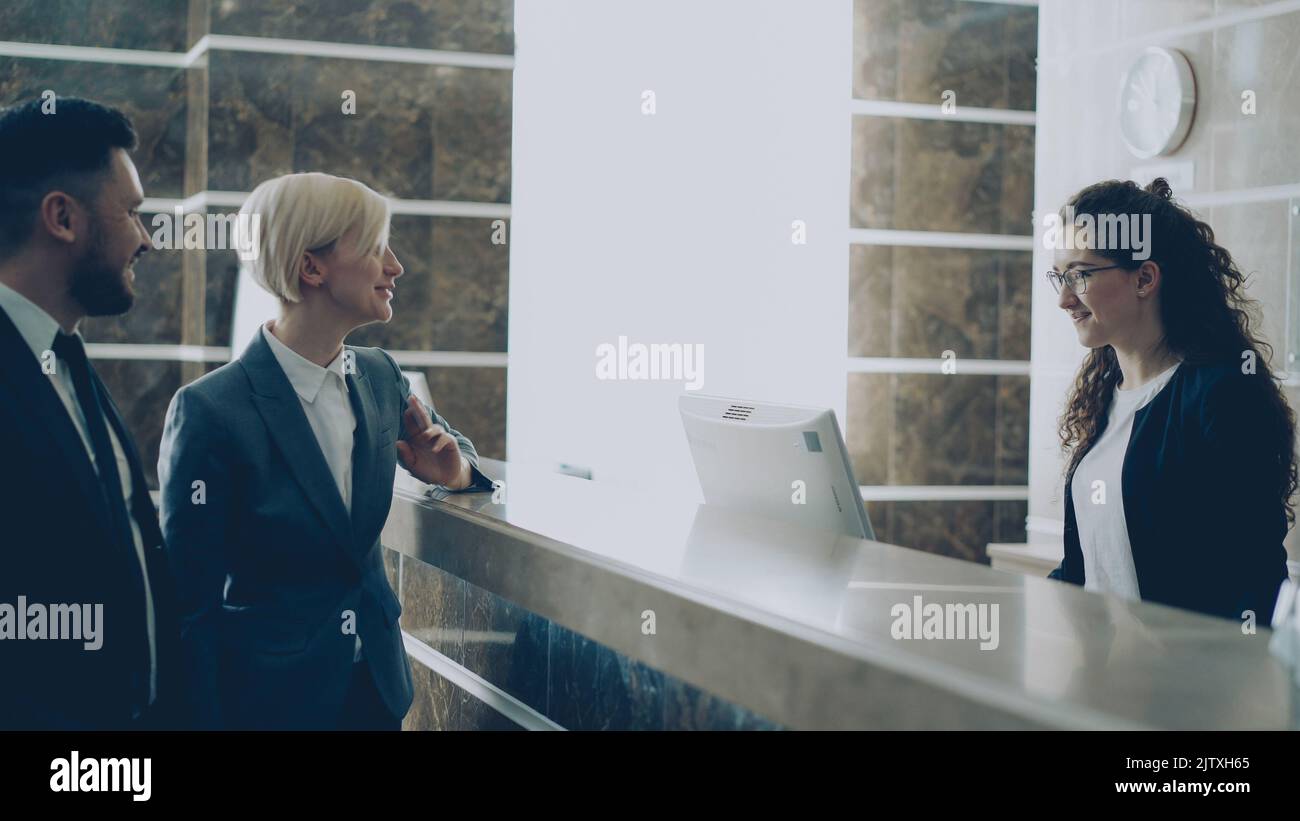 Receptionist talking with arrived businessman and businesswoman guests ...