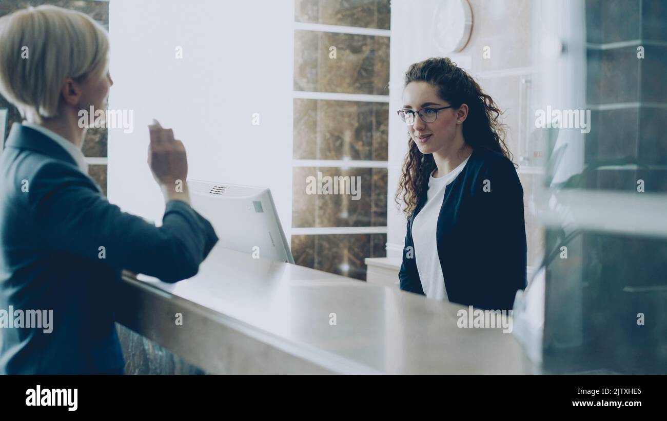 Blonde businesswoman with luggage talking with staff at reception in ...