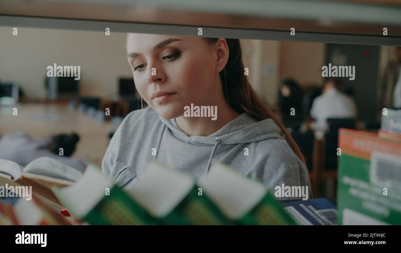 Young caucasian beautiful female student is standing near shelf with ...