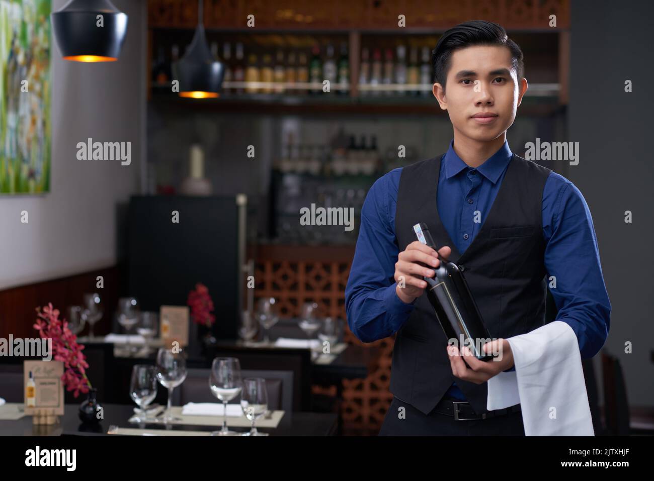 Handsome young Vietnamese waiter offering you a bottle of red wine ...