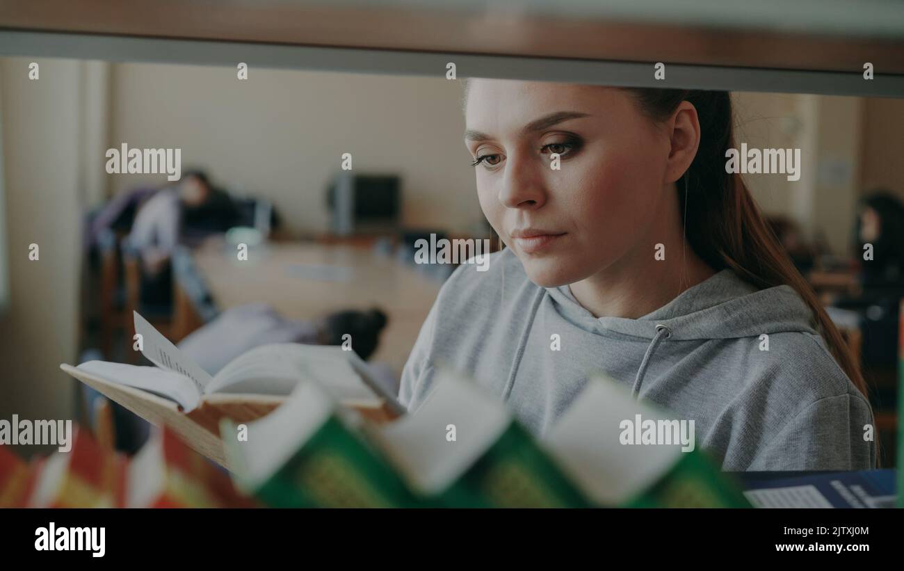 Young caucasian beautiful female student is standing near shelf with ...