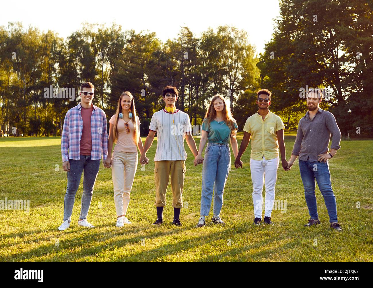 Company of friendly multiracial young people holding hands standing in ...
