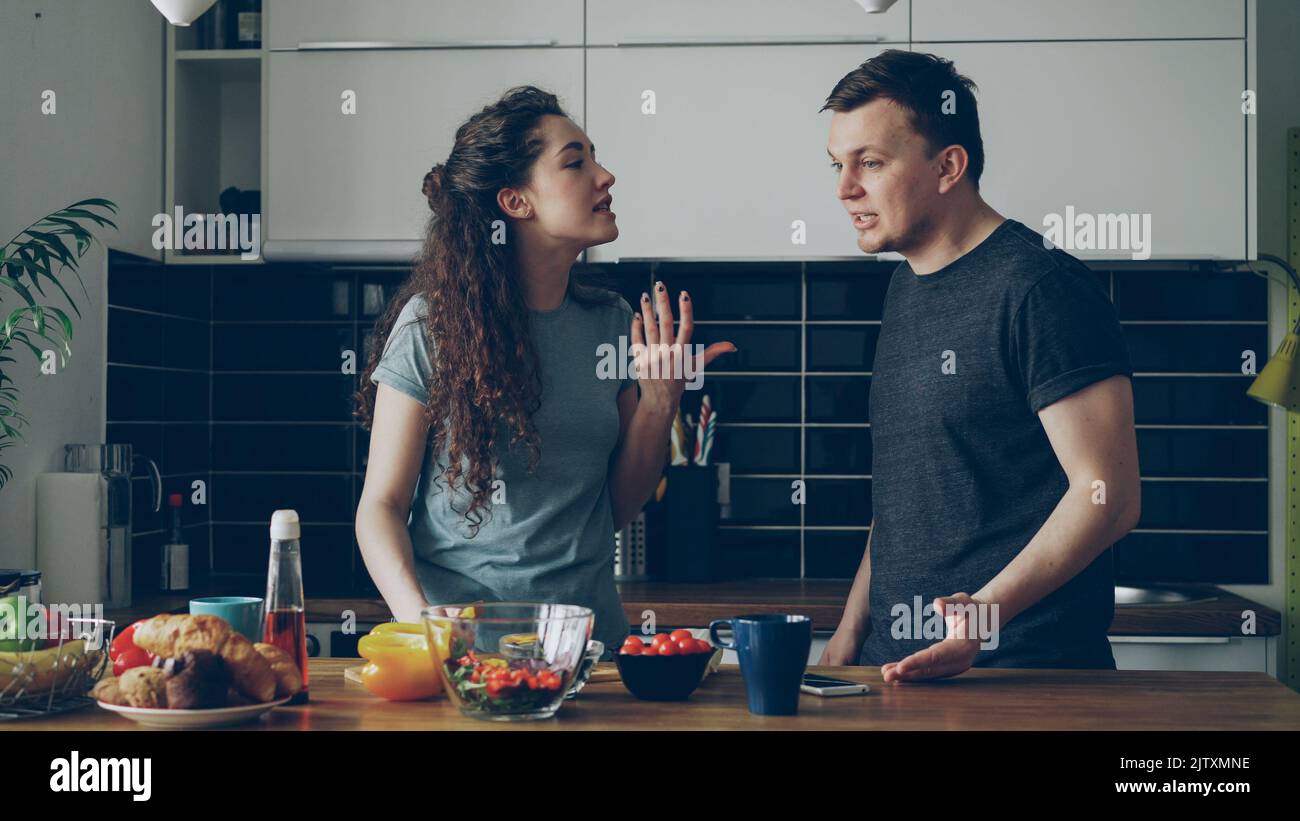 Pretty woman standing at table cutting salad while her boyfriend comes ...