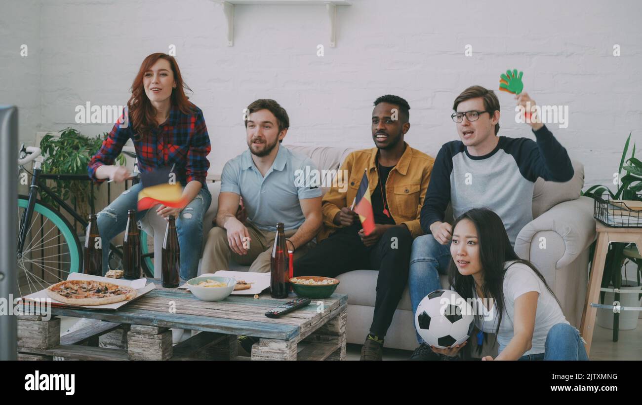 Happy friends with German flags watching sports championship on TV ...