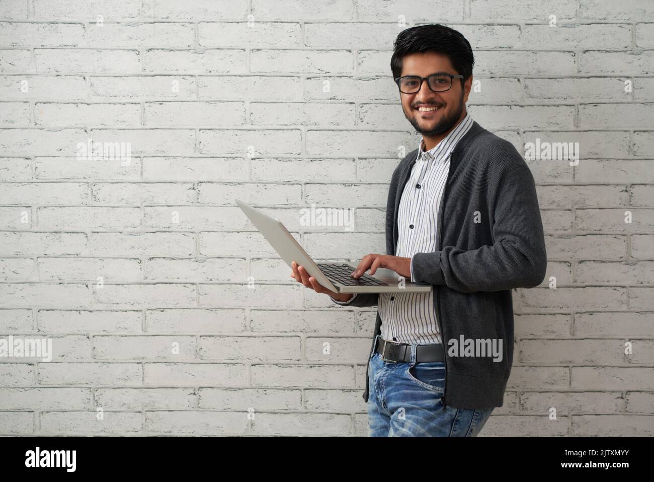 Portrait of cheerful Indian programmer with laptop standing against ...