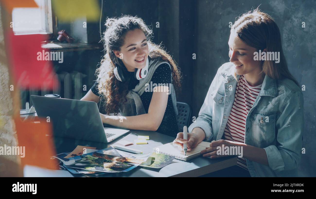 Cheerful pretty girl is working with laptop and listening to music ...