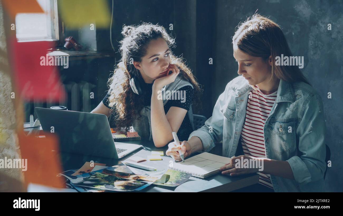 Cheerful pretty girl is working with laptop and listening to music ...
