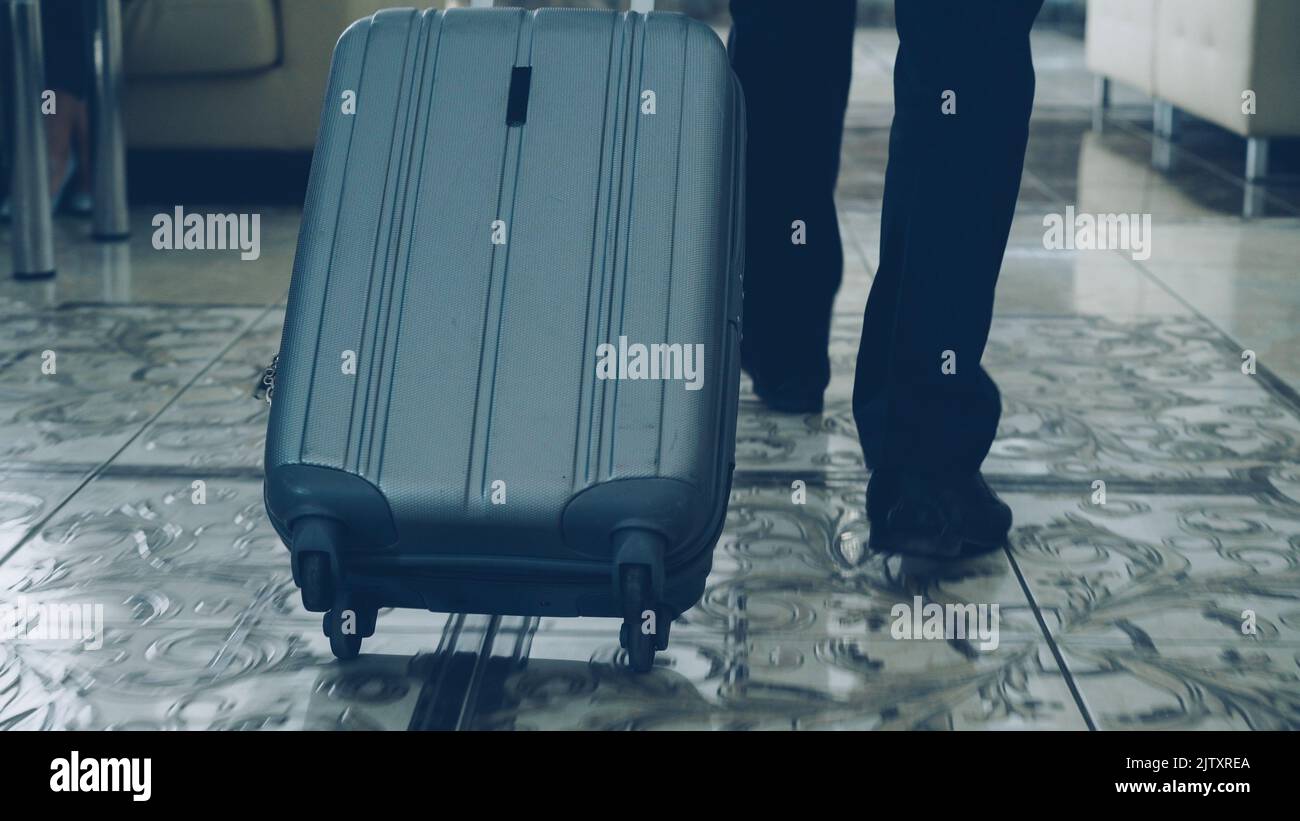 legs of businessman walking through hotel lobby pulling luggage and ...