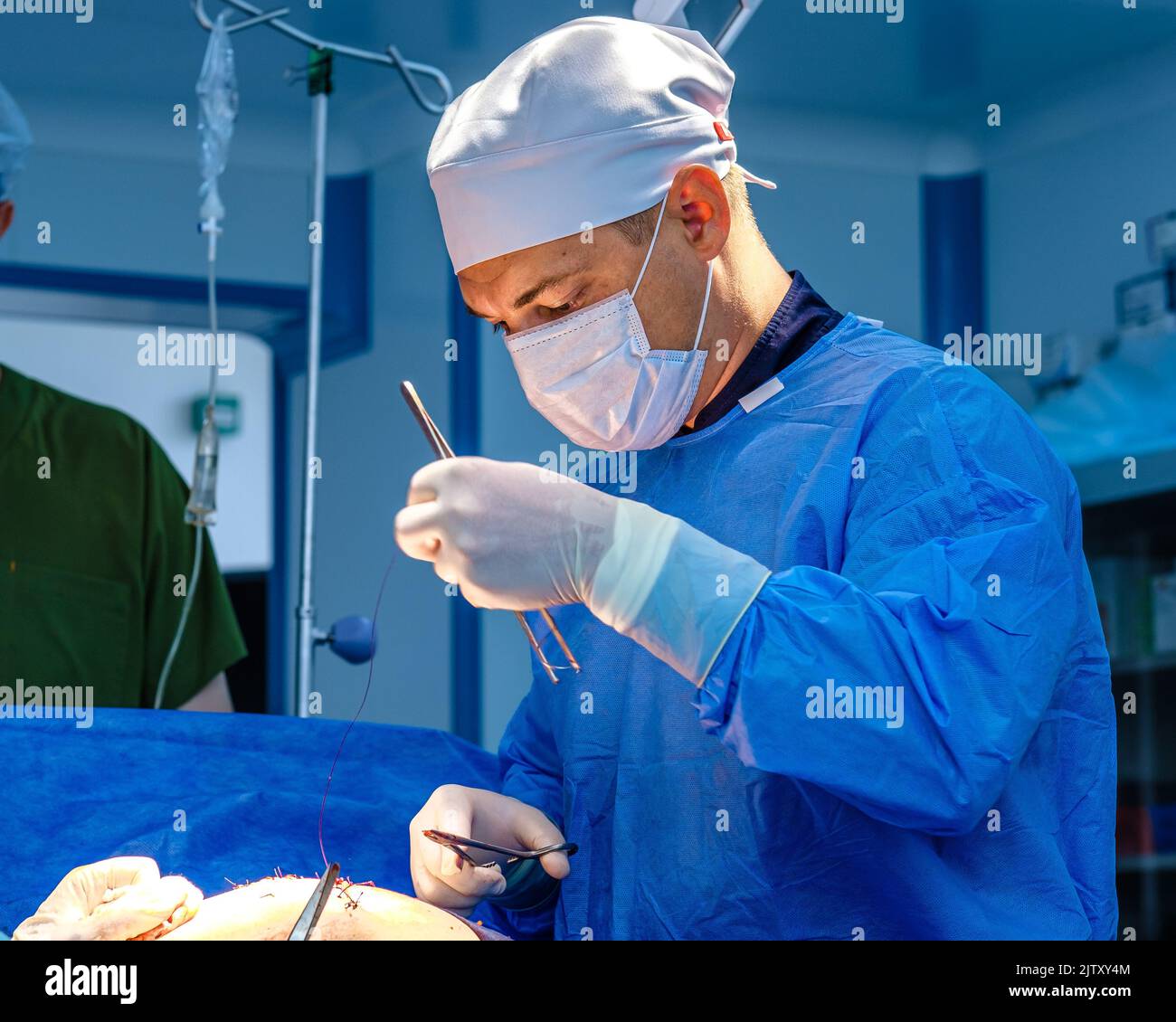 A male surgeon during surgery sews up the patient's skin with surgical ...