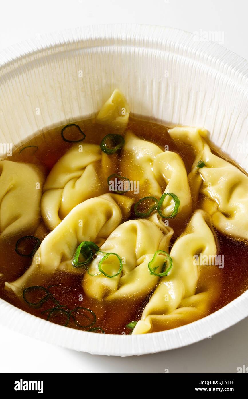 asian steamed dumplings served in chili broth on a white table in a box ...