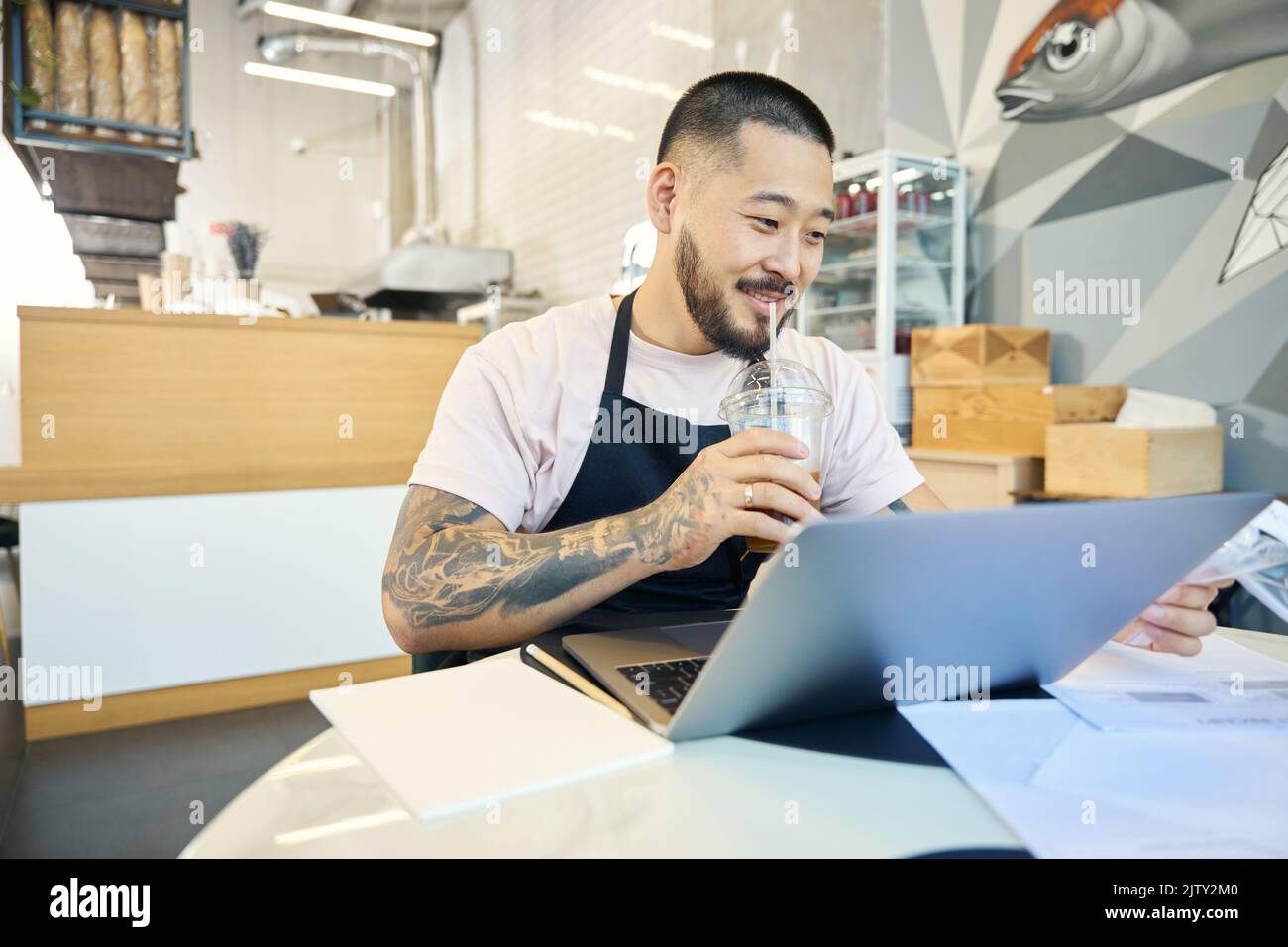Good-looking barista working on his laptop inside coffee joint Stock ...
