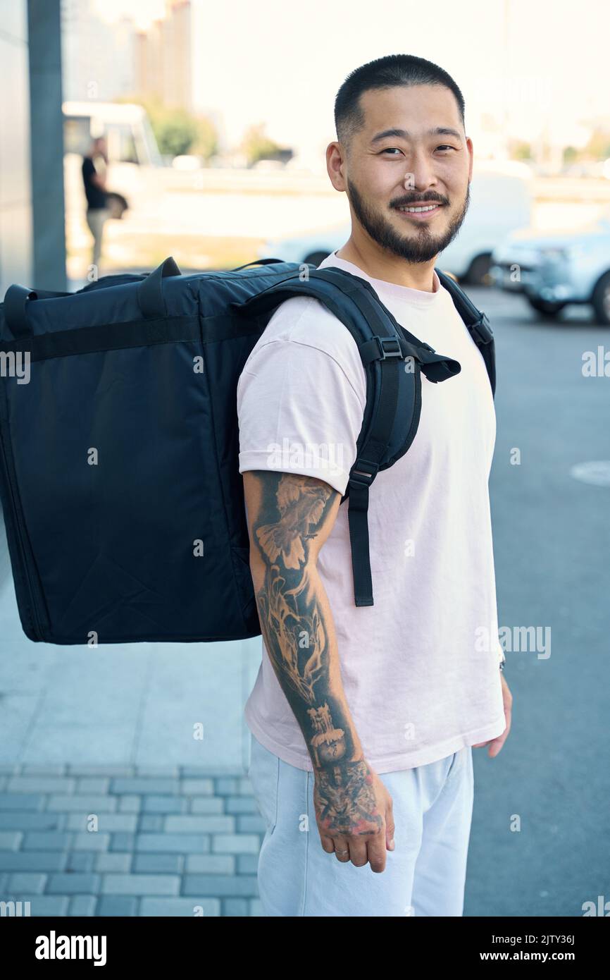 Joyous food delivery man smiling and posing in the street Stock Photo ...
