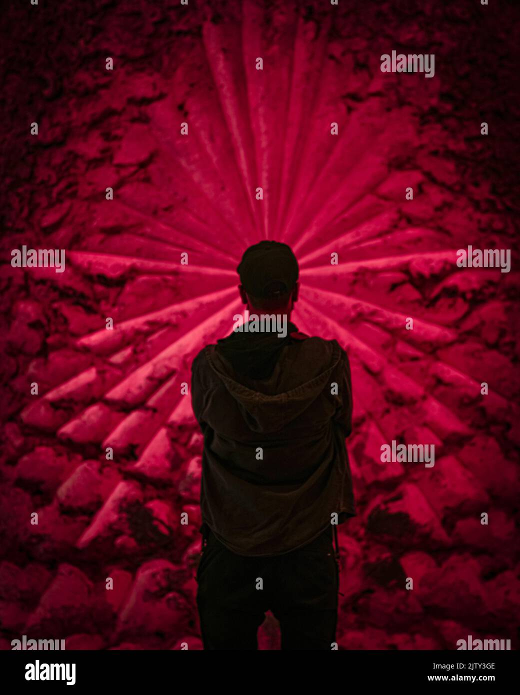 A vertical shot of a silhouette of a man posing in front of a red wall ...