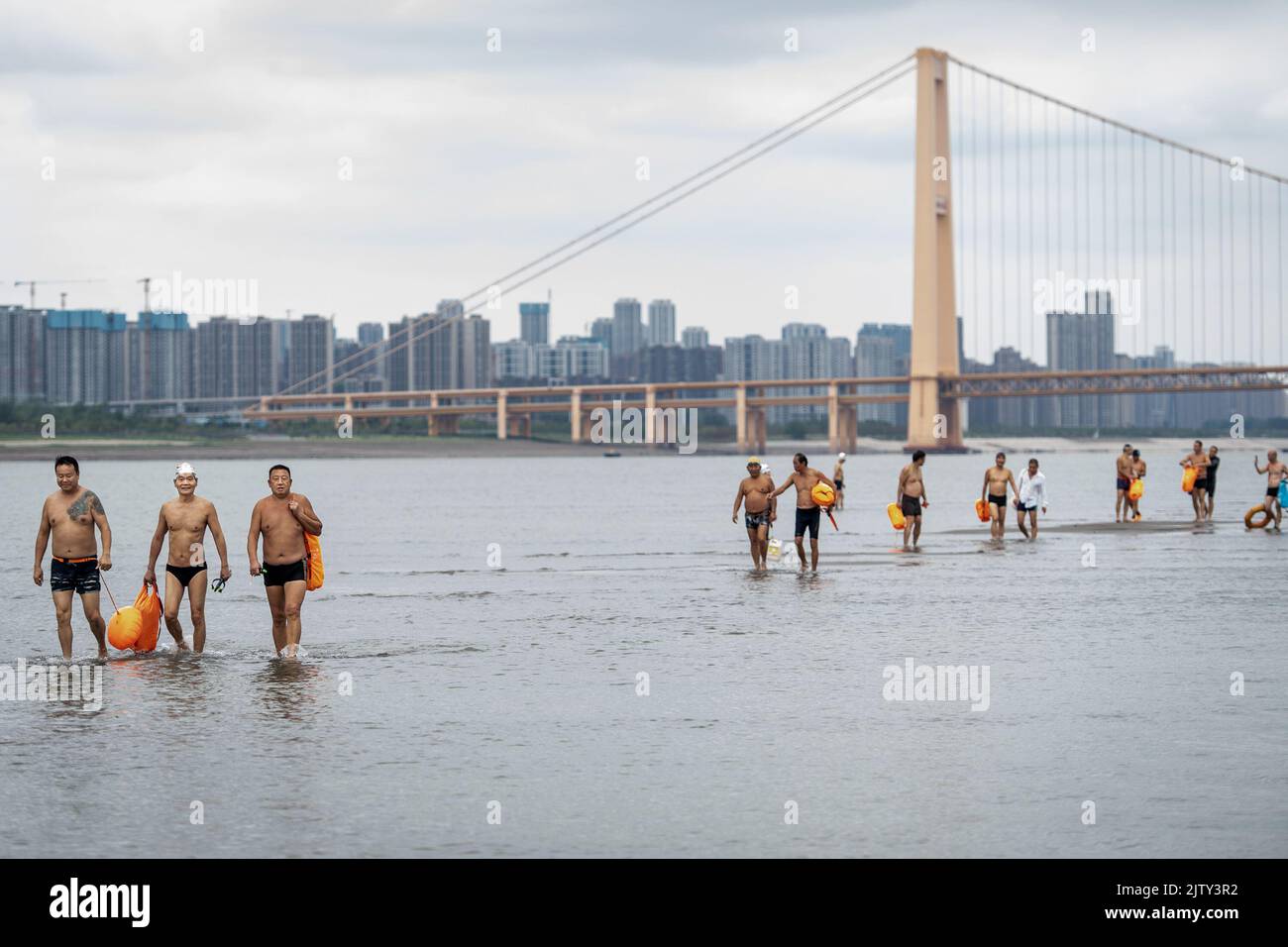 Swimmers walk along dry riverbed besides a wing dam in the middle of ...