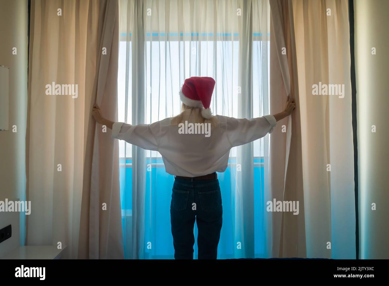 Young woman in a Santa Claus hat in a white shirt and blue jeans opens ...