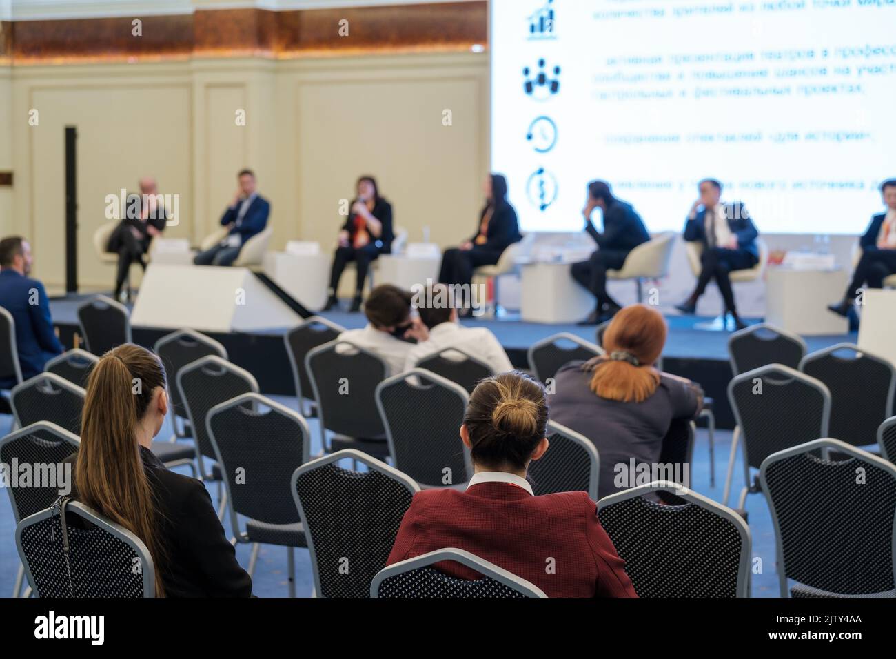Back view of anonymous people sitting on chairs and listening to ...