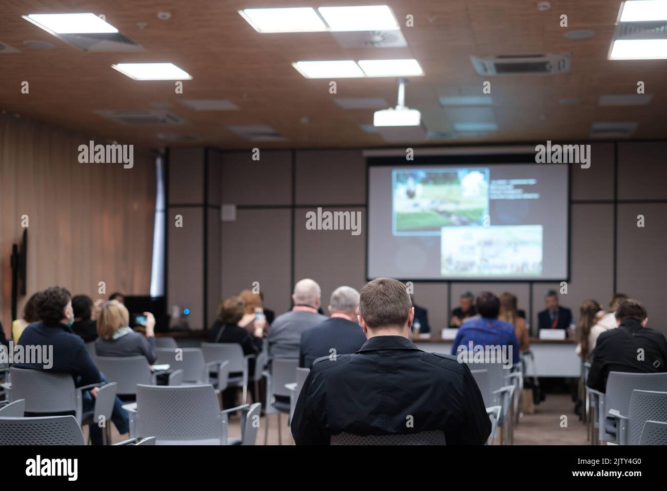 Back view of anonymous people sitting on chairs and listening to ...