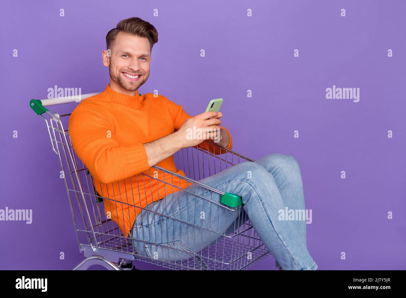 Photo of positive handsome shopaholic man sit in pushcart surfing in ...