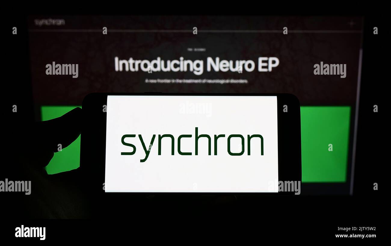 Person holding smartphone with logo of American brain interface company Synchron Inc. on screen ...
