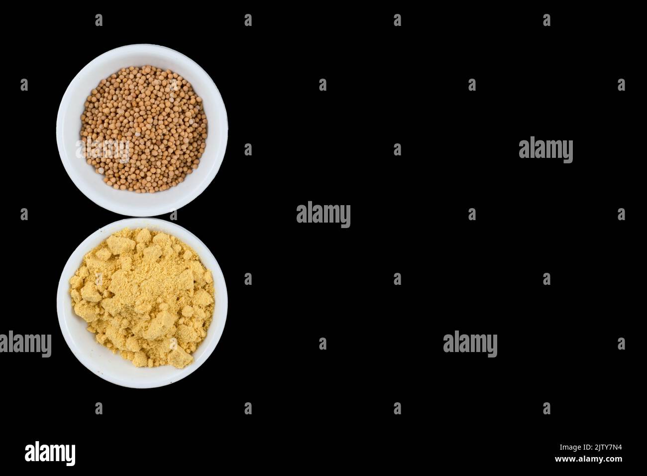 brown Mustard seeds and yellow mustard powder in white bowls on a black ...