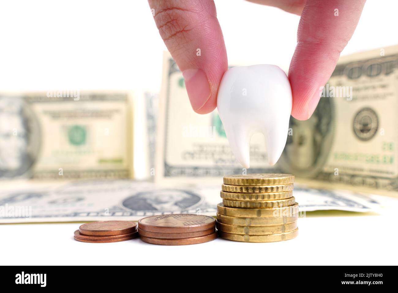 Pinch-holding a large white tooth above coin stacks against dollar ...
