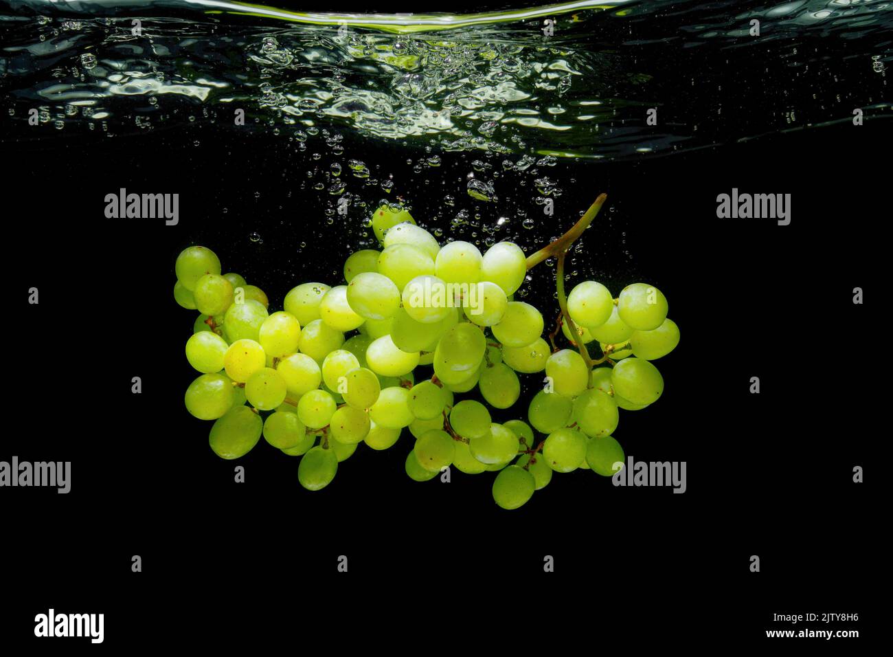Bunch of white grapes sinking underwater isolated on black background ...