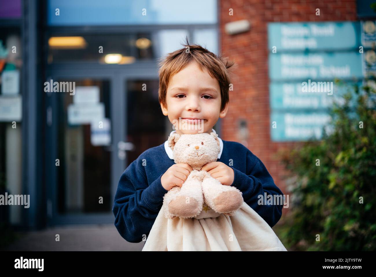 Cute primary school pupil holding teddy bear at the school entance ...