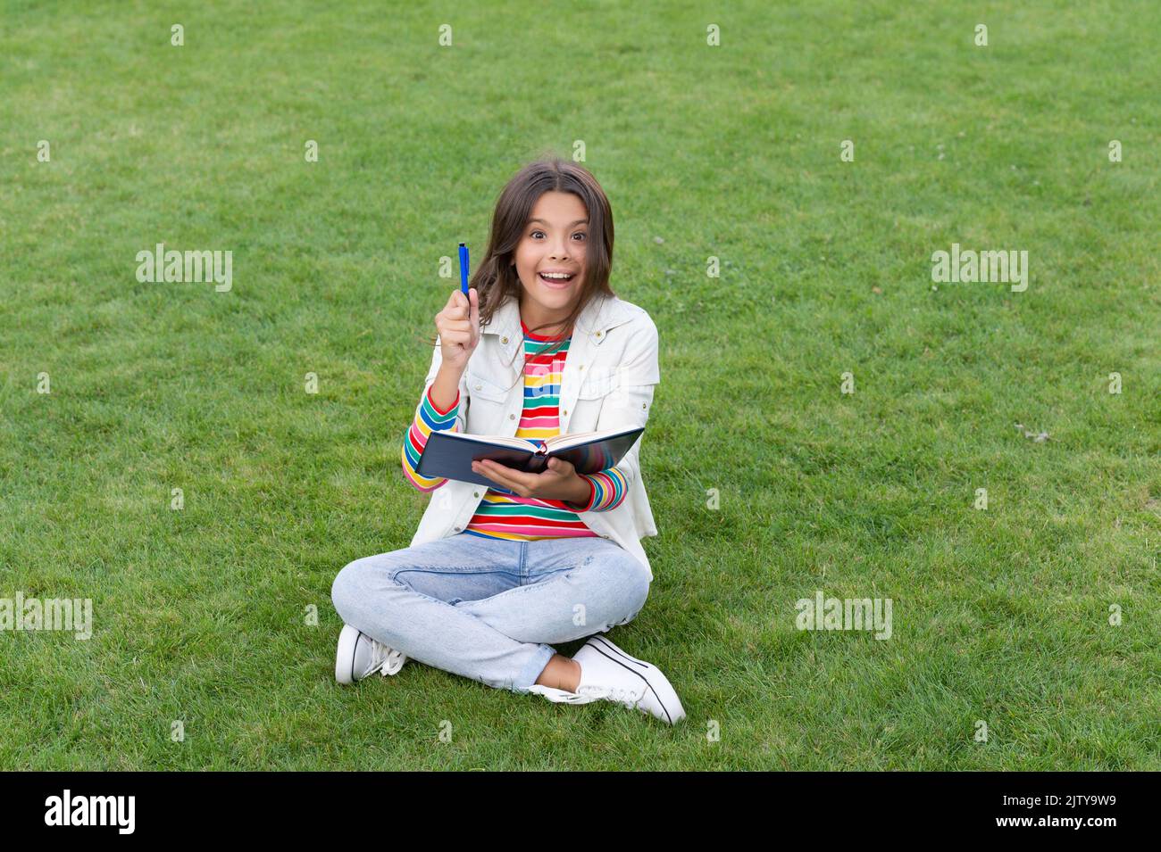 surprised teen girl making notes in notebook sitting on grass. taking ...